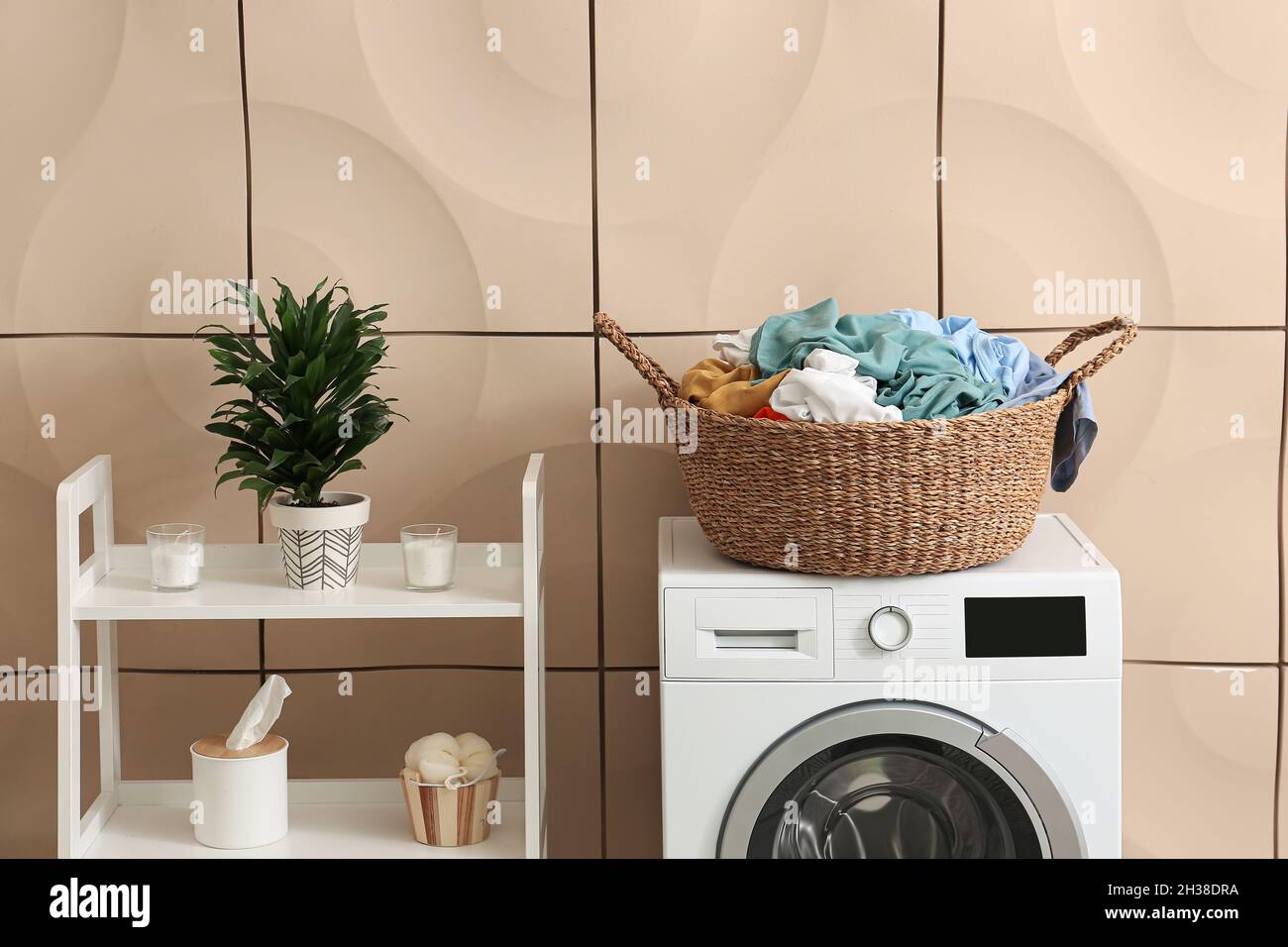 Washing machine, basket with laundry and shelving unit near beige wall ...