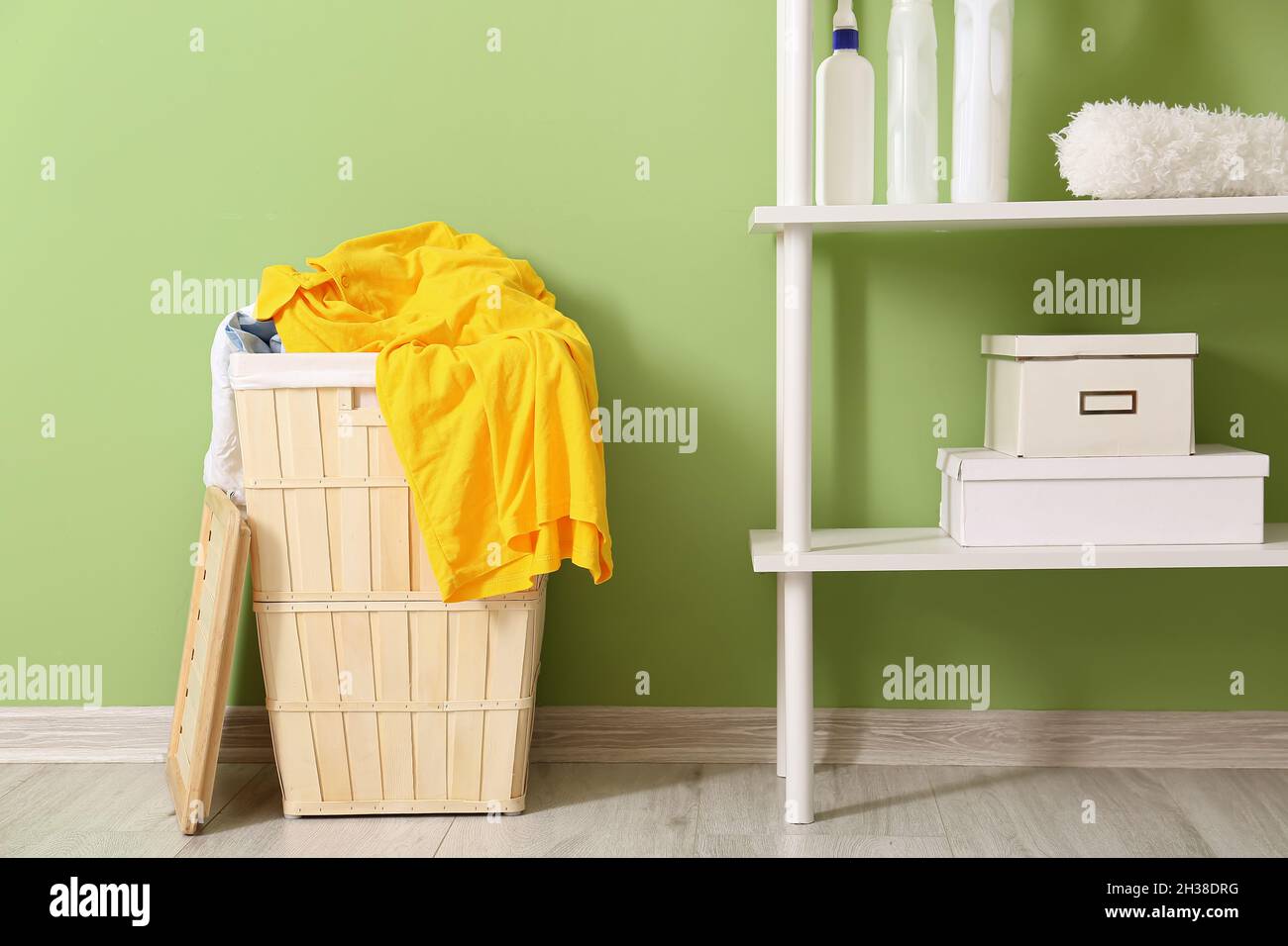 Wooden basket with dirty clothes and shelving unit near green wall ...