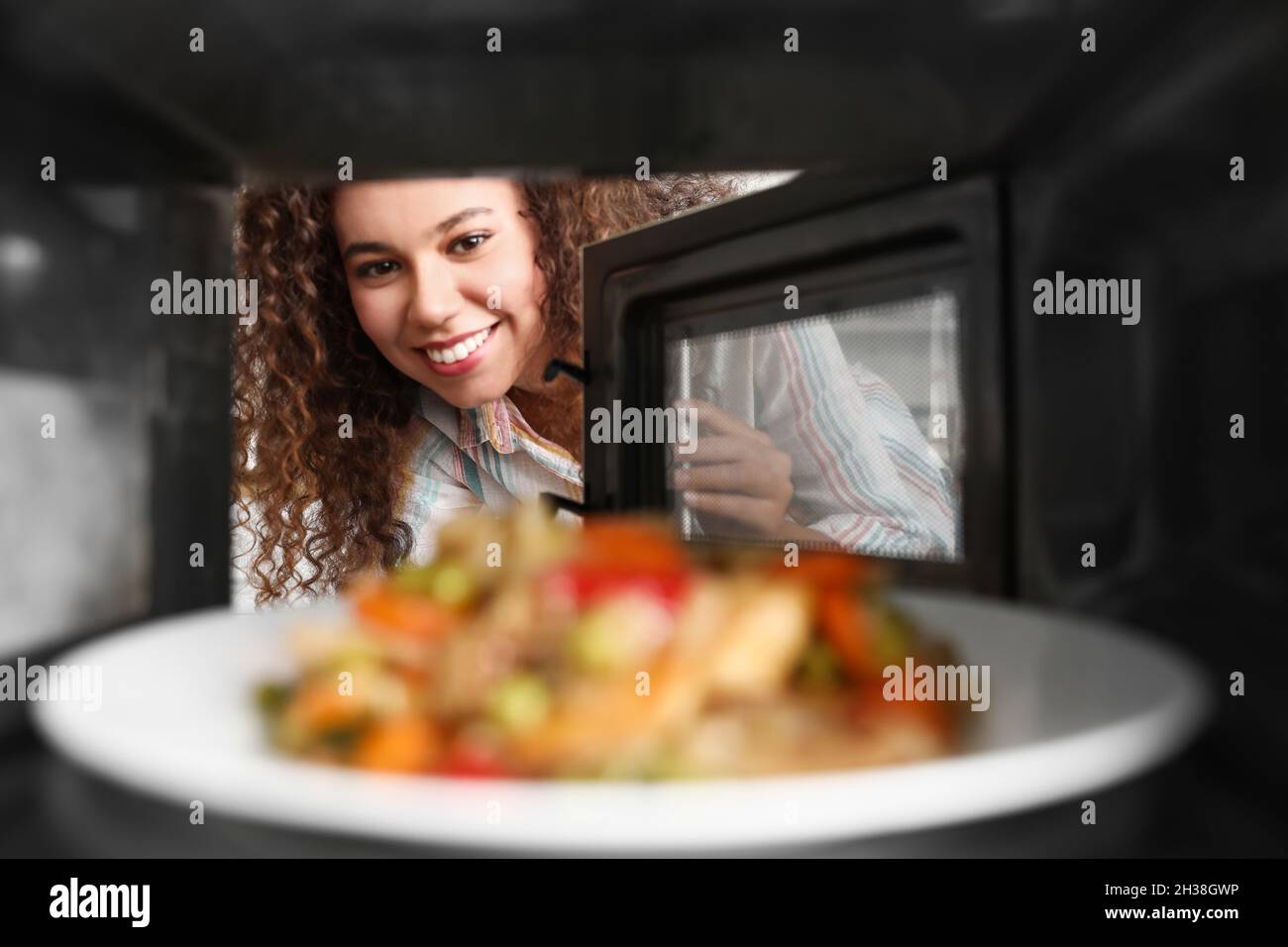 Young African-American woman heating food in microwave oven, view from ...