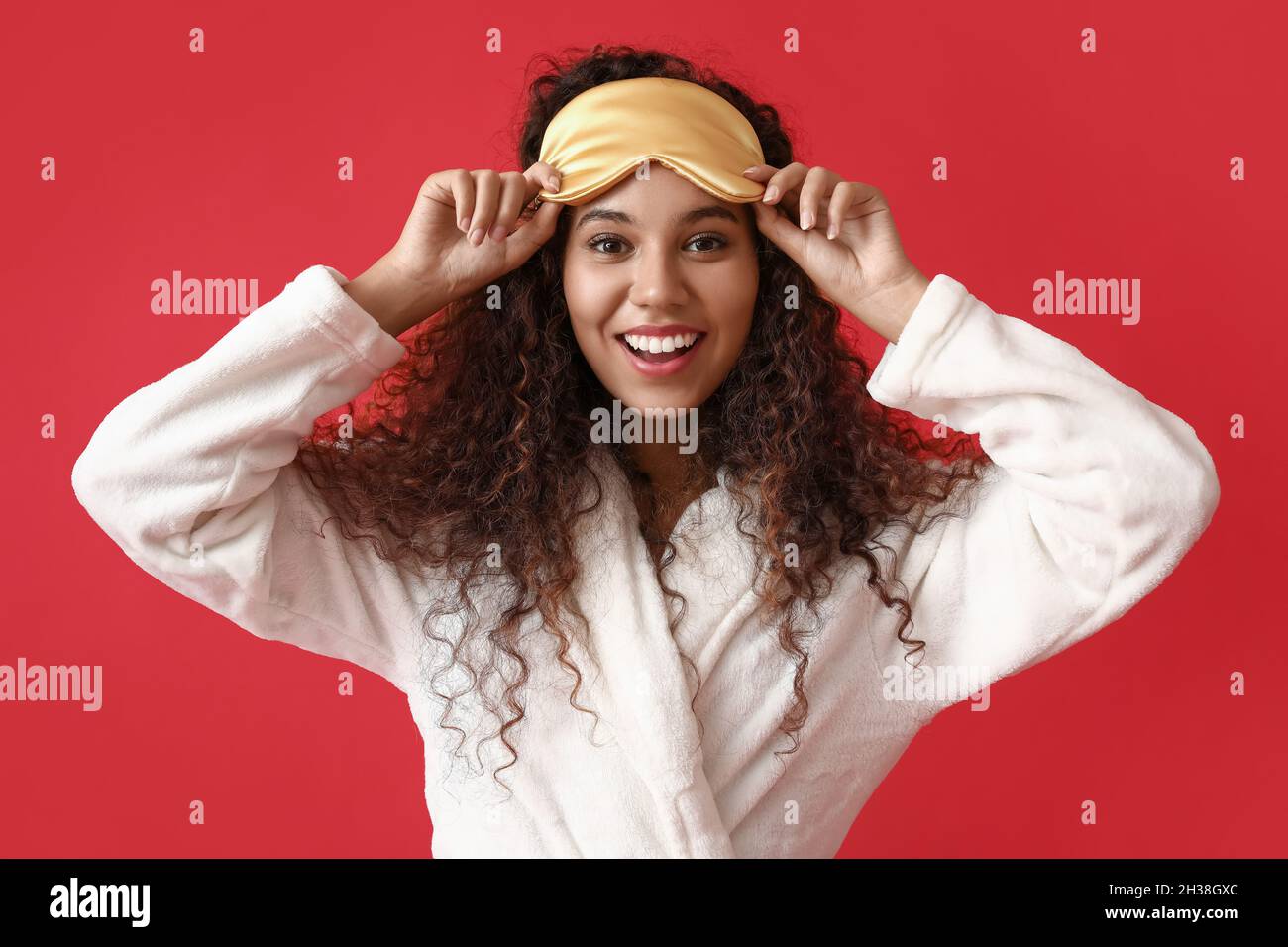 Young African-American woman with yellow sleeping mask on red ...