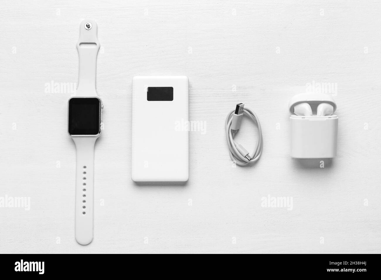 Modern power bank, smartwatch and earphones on white wooden background ...