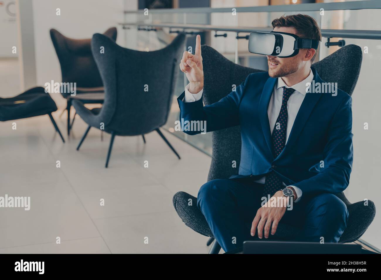 Young CEO sitting in office centre lobby with VR headset goggles ...