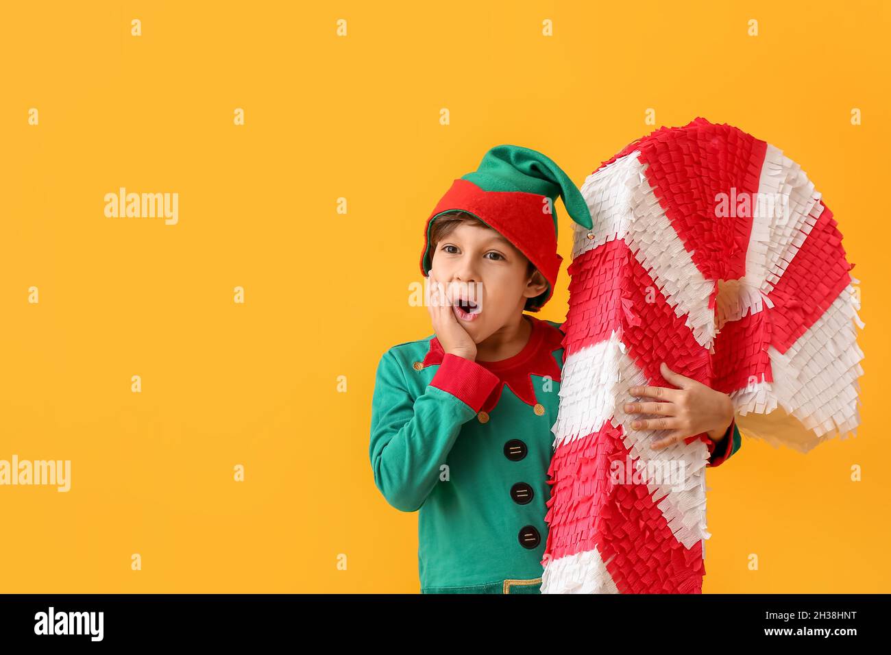 Cute little boy dressed as elf with candy cane pinata on color ...