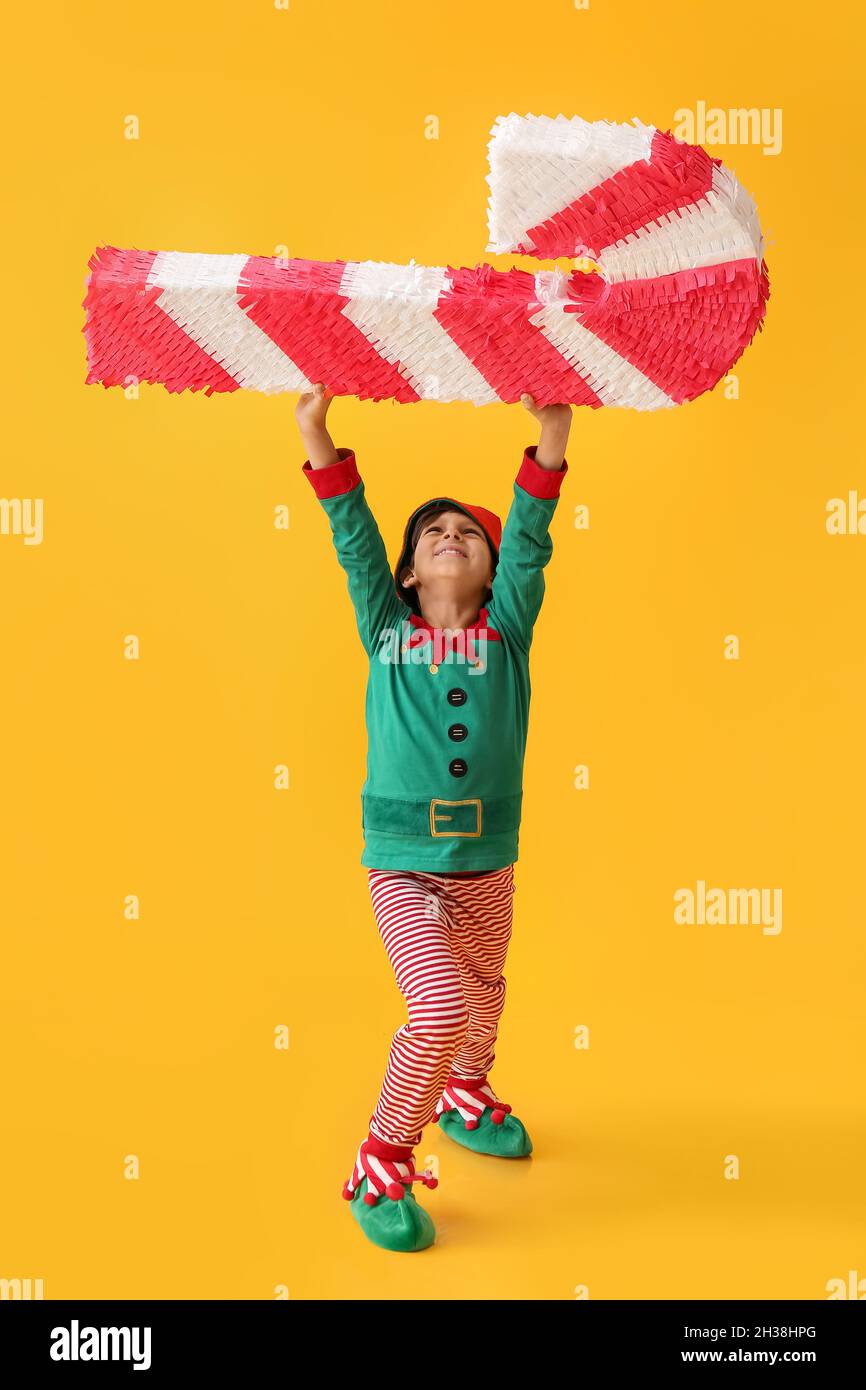 Cute little boy dressed as elf with candy cane pinata on color ...