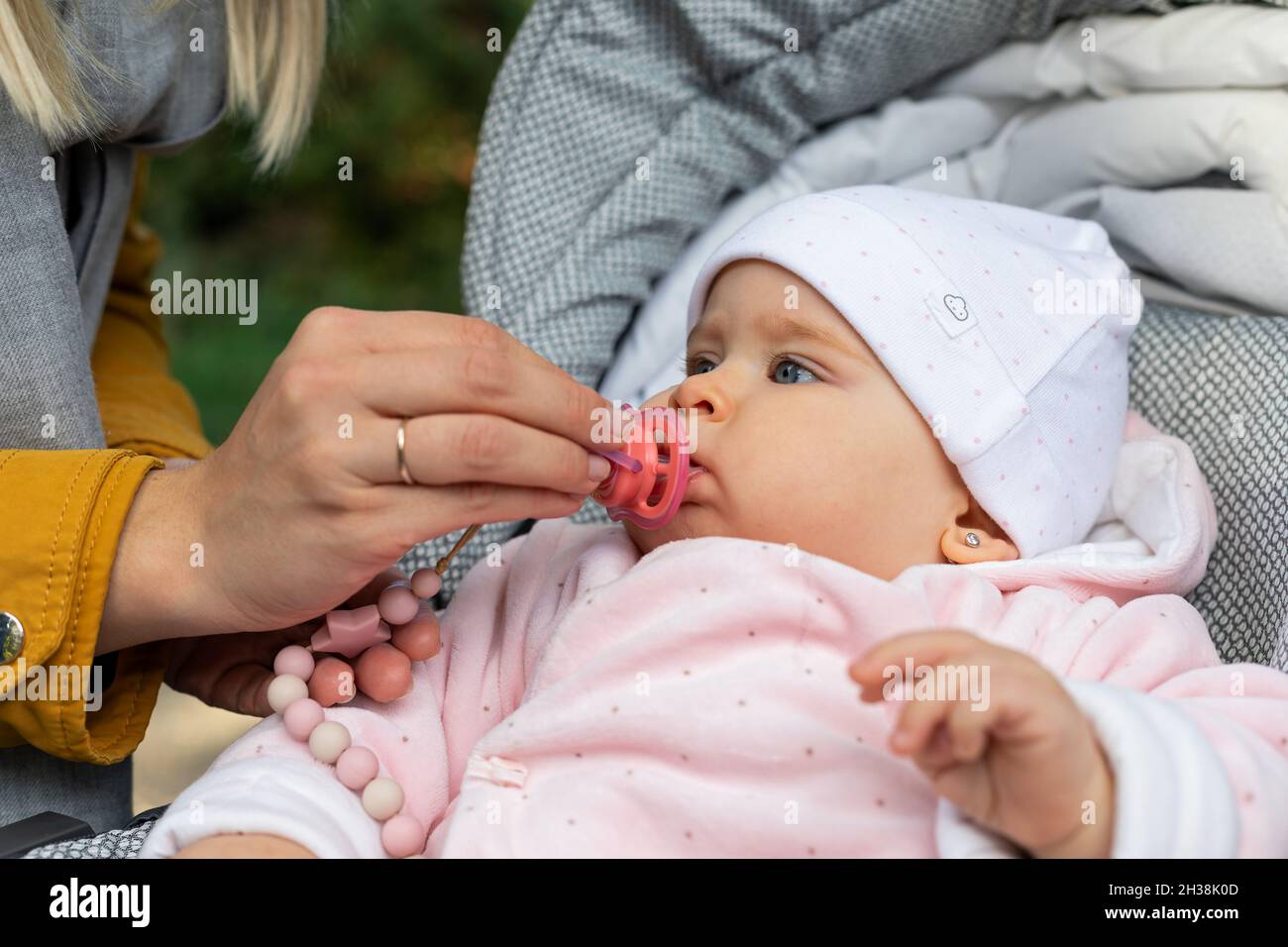 Baby girl with a pacifier in his mouth sitting in a stroller outdoor ...