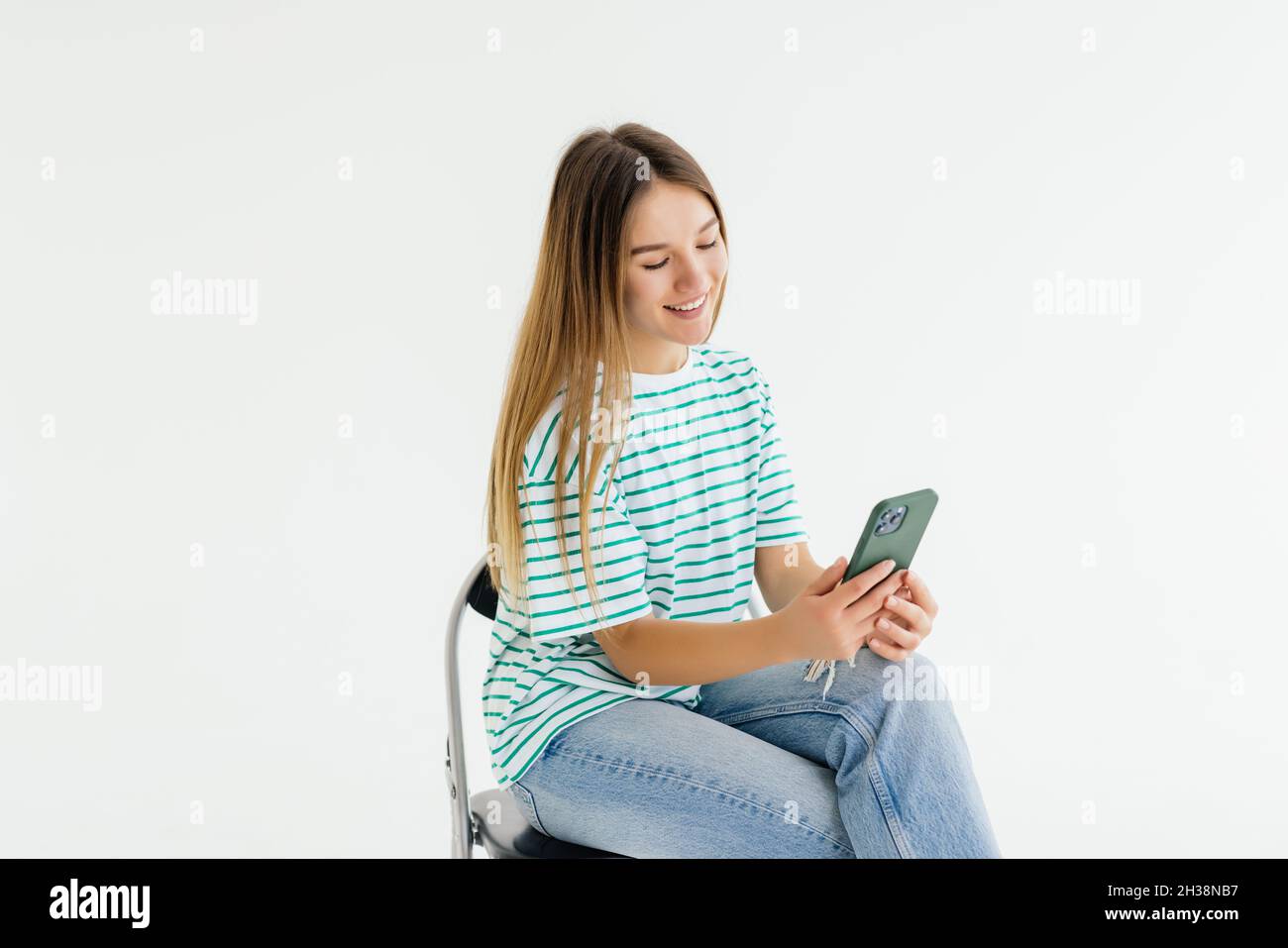 Portrait of cute woman sitting on white chair and texting on the phone ...