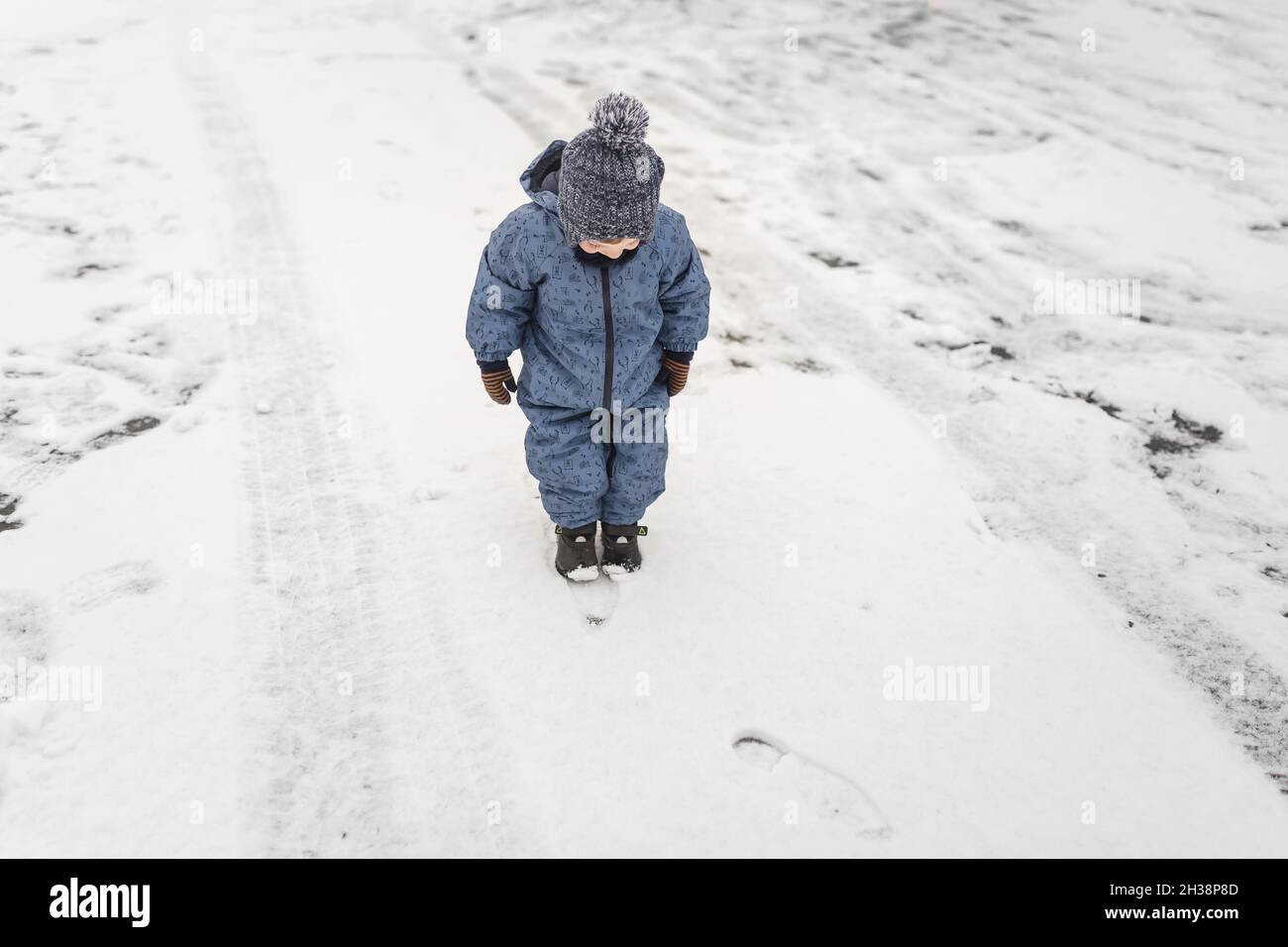 Little boy outside in warm blue onesie and hat looking at his fe Stock ...