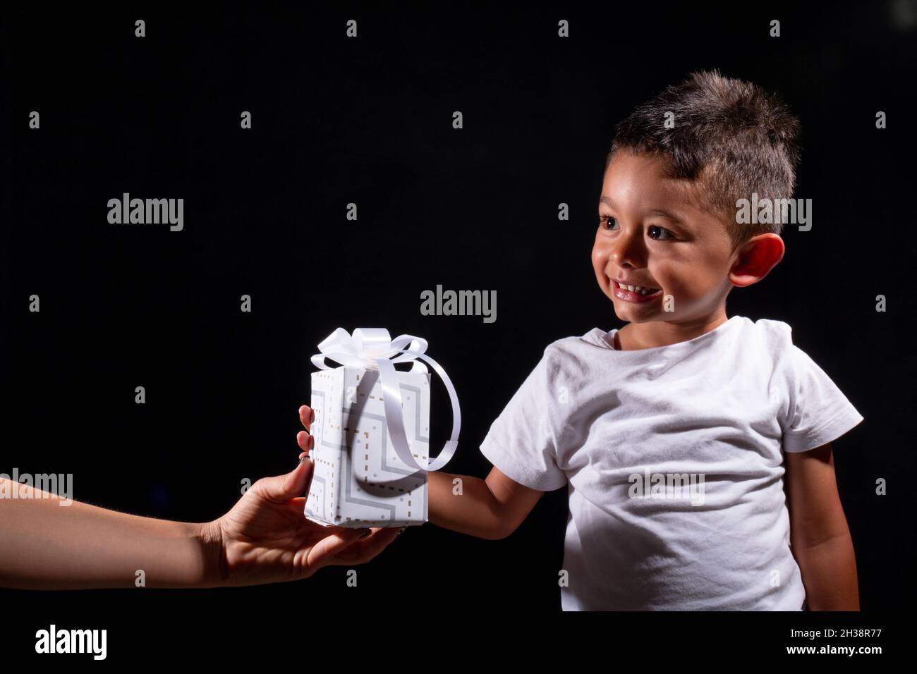 Child receiving gift from his mother, black background. Woman hand ...