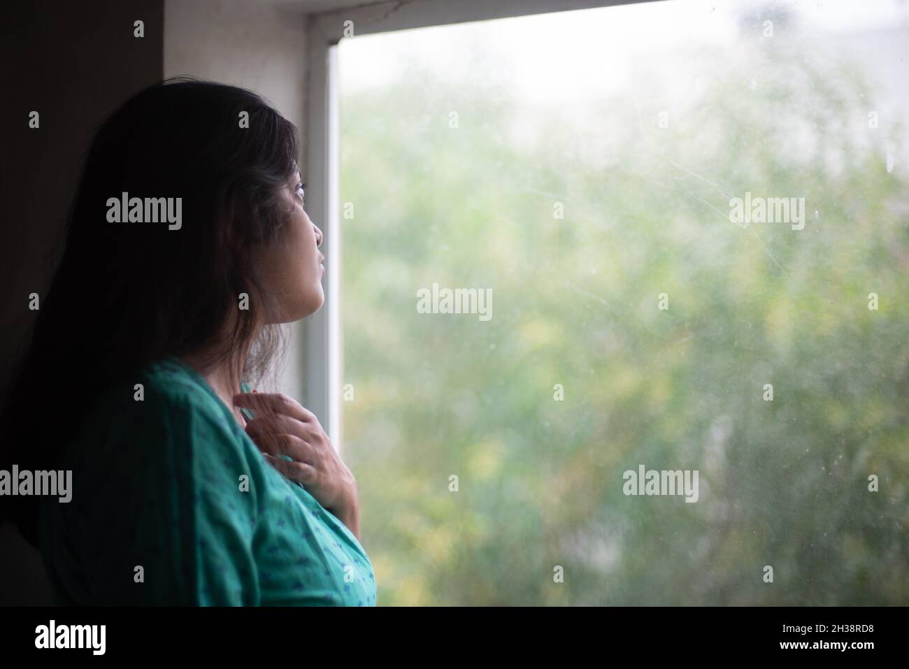 Young woman wearing green dress looking outside through window Stock ...