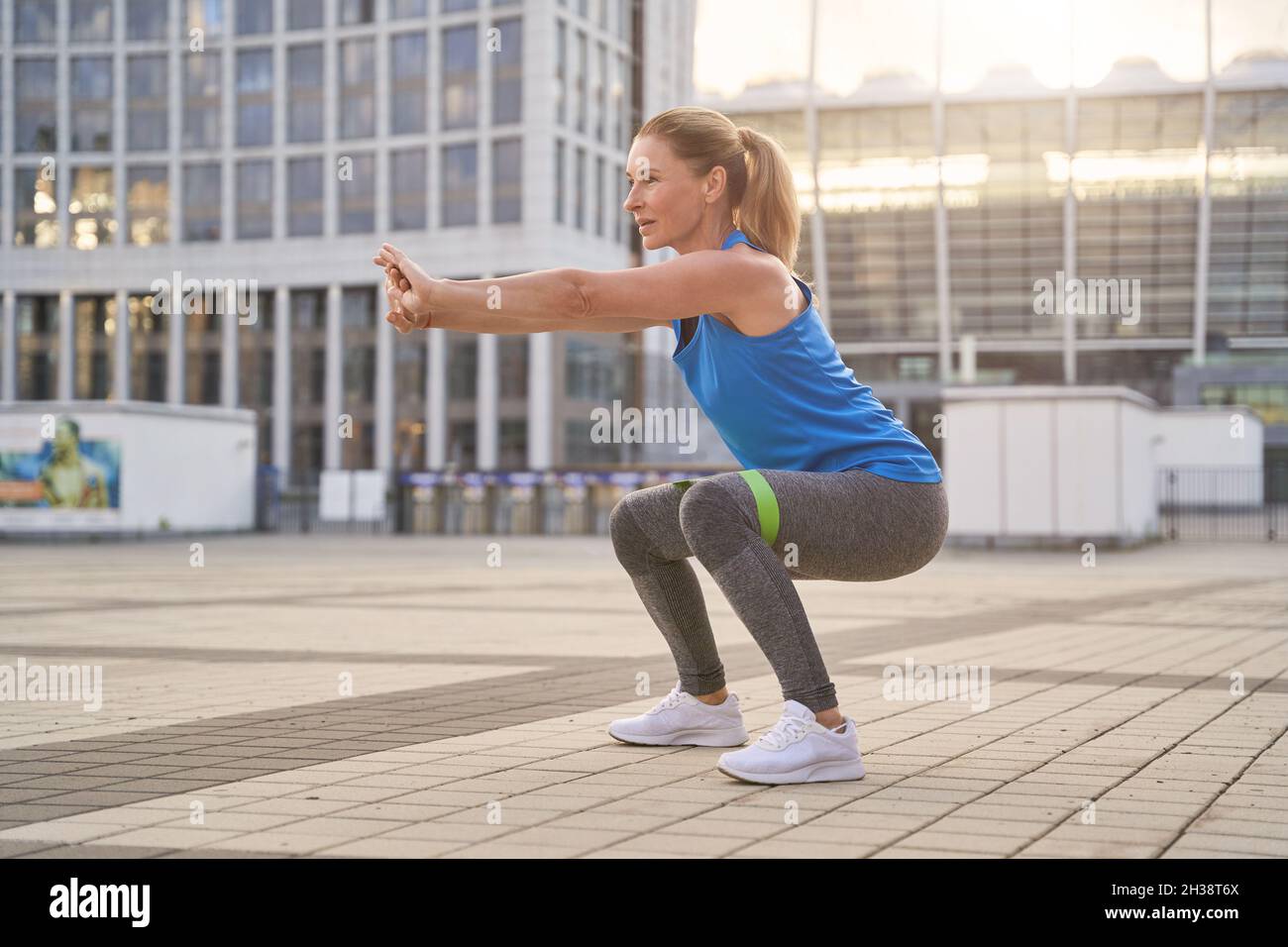 Attractive middle aged woman in sportswear doing squats using ...
