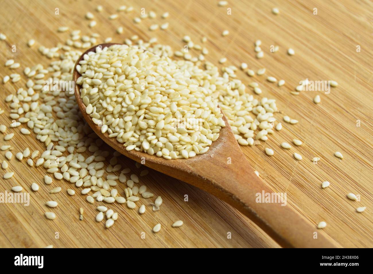 Organic fresh raw sesame seeds, in wooden spoon on bamboo cutting board ...