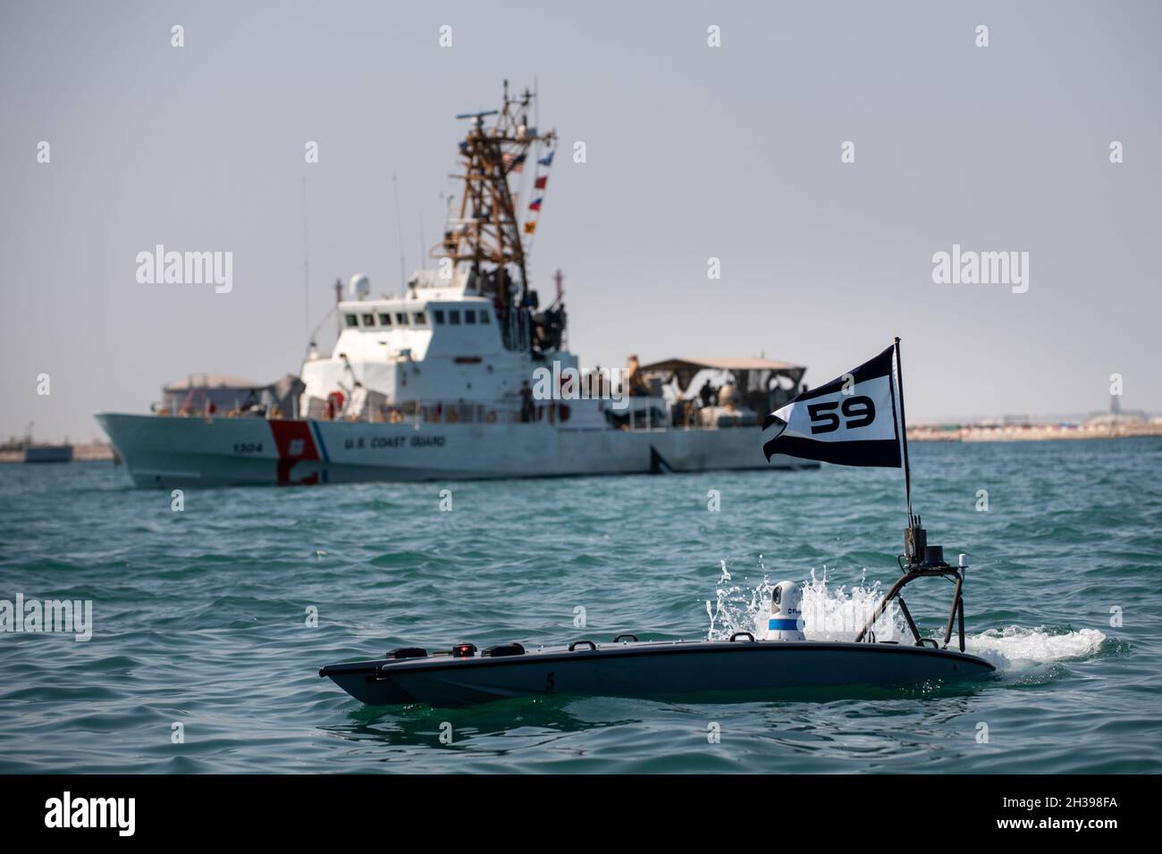 A MANTAS T-12 unmanned surface vessel (USV), front, operates alongside ...