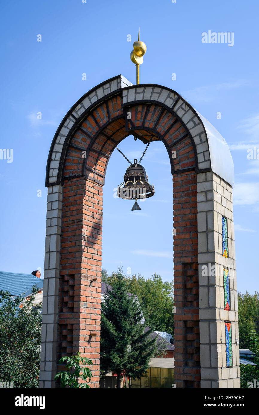 A brick arch with a bell and a spire near the Temple of All Religions ...
