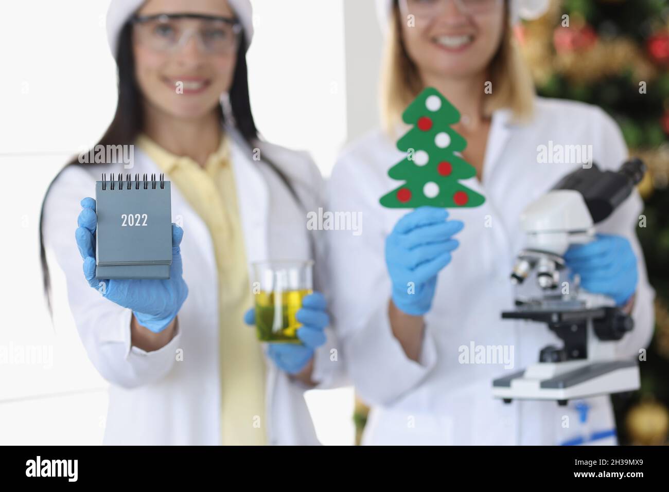 Female chemists holding microscope and calendar for 2022 near new year ...