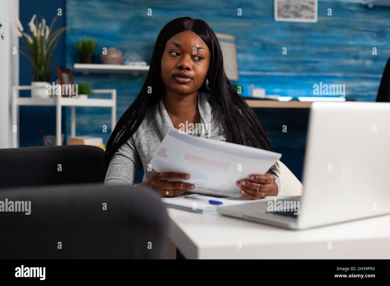 Worker looking at laptop display and holding papers with data charts ...