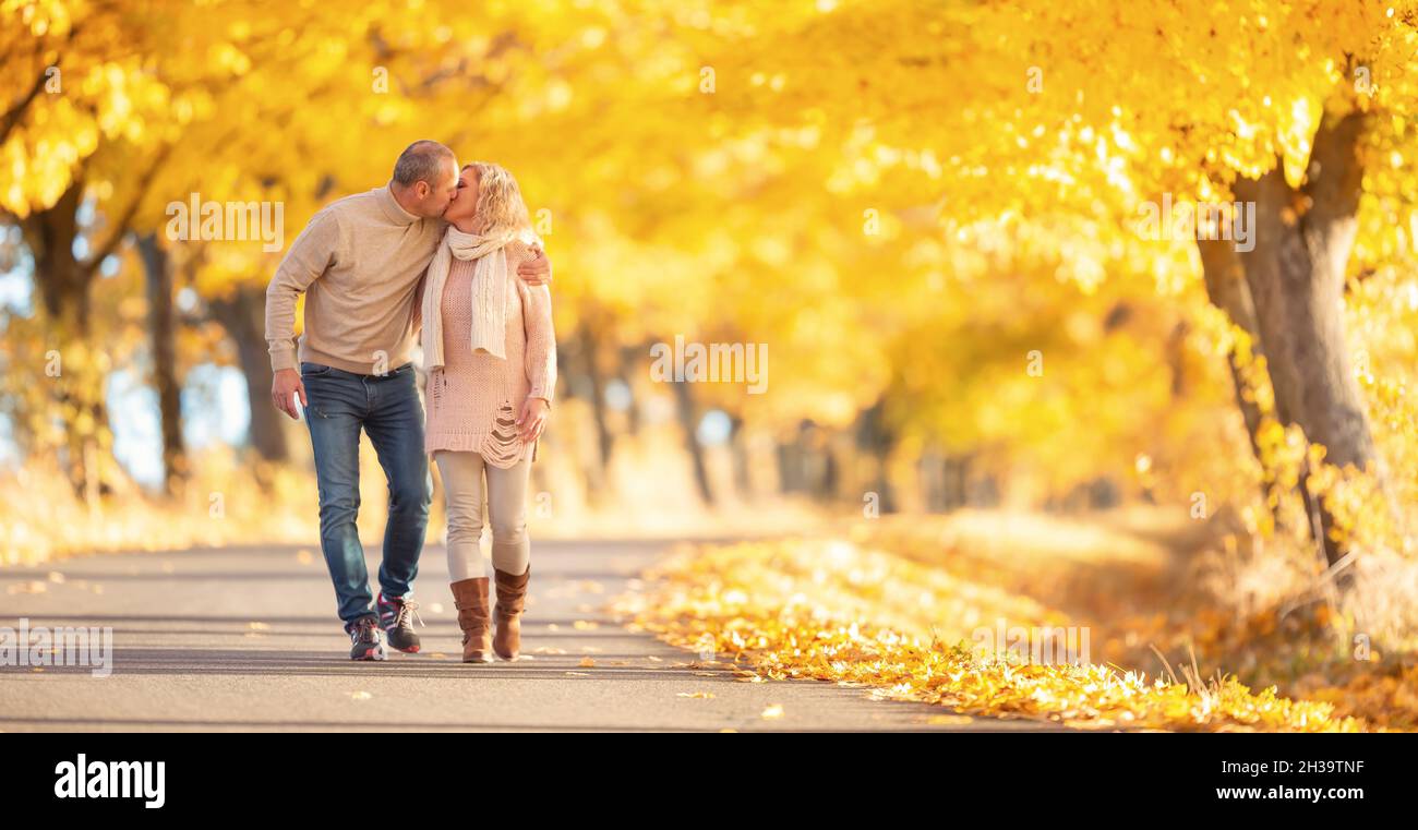 An adult couple in love with kisses walking through a beautiful autumn ...