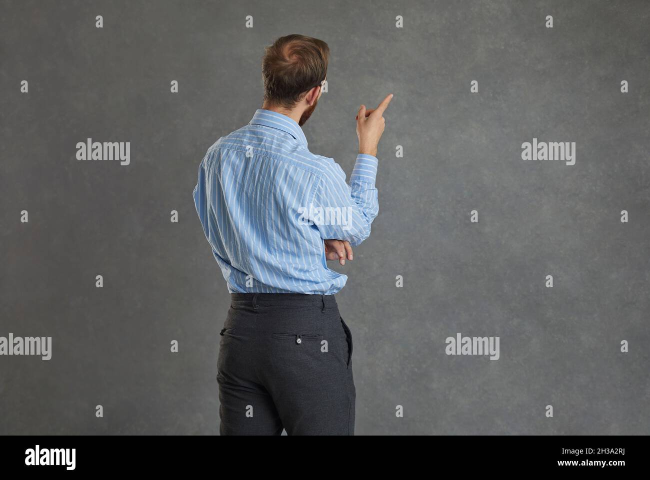 Focused businessman turned his back to the camera standing on a gray ...