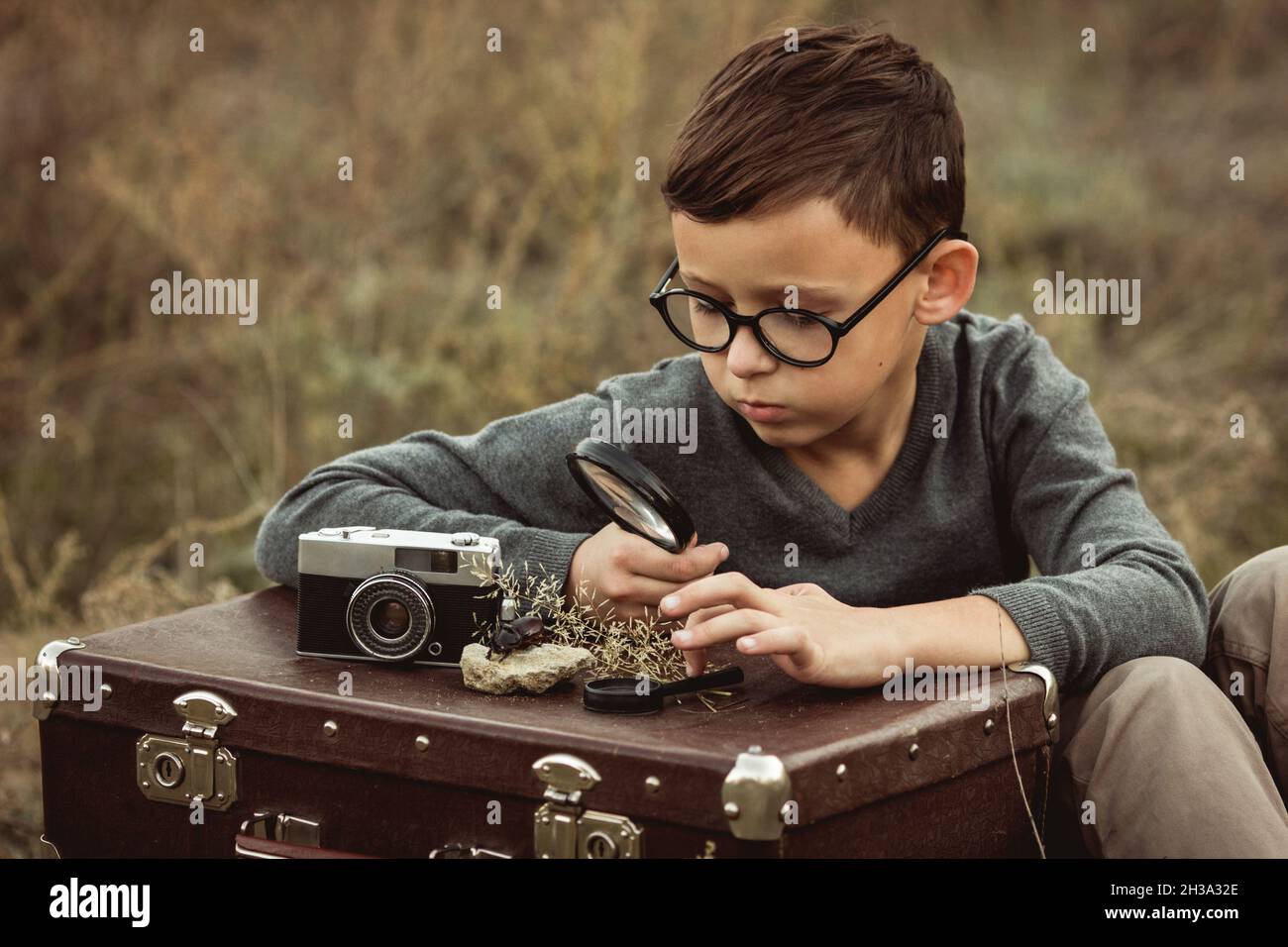 Boy with camera on walk examines beetle under magnifying glass ...