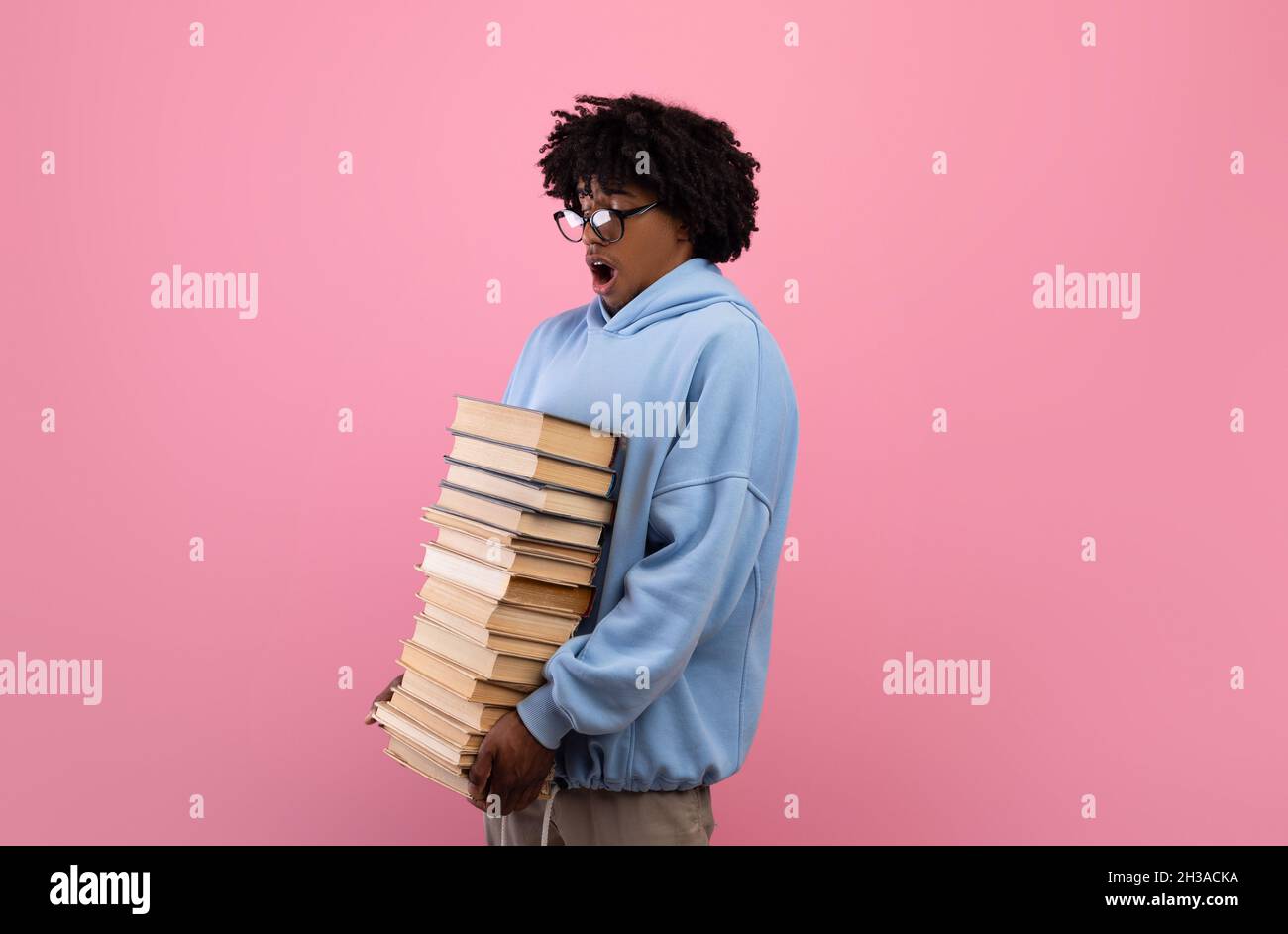 Overwhelmed black teenage student holding big stack of books, having ...