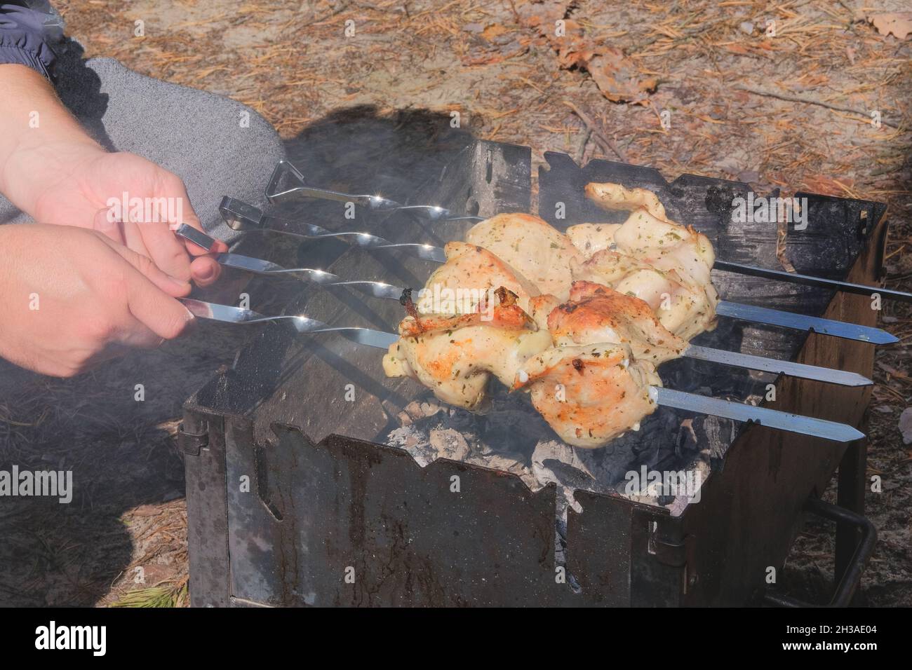 Man roasts chicken meat outdoors in the forest. Meat frying on grillin ...