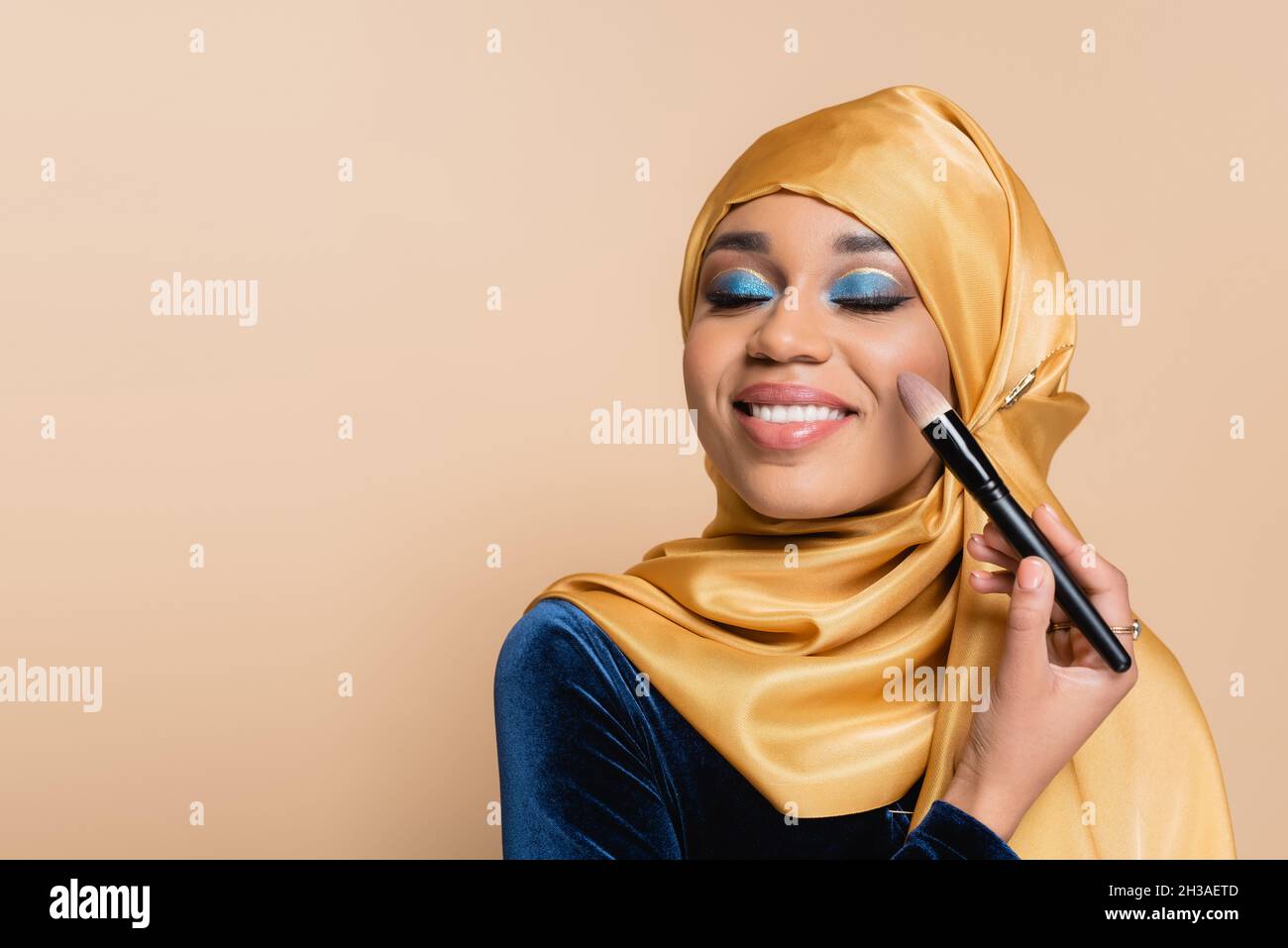 happy muslim woman in yellow hijab applying makeup foundation with ...