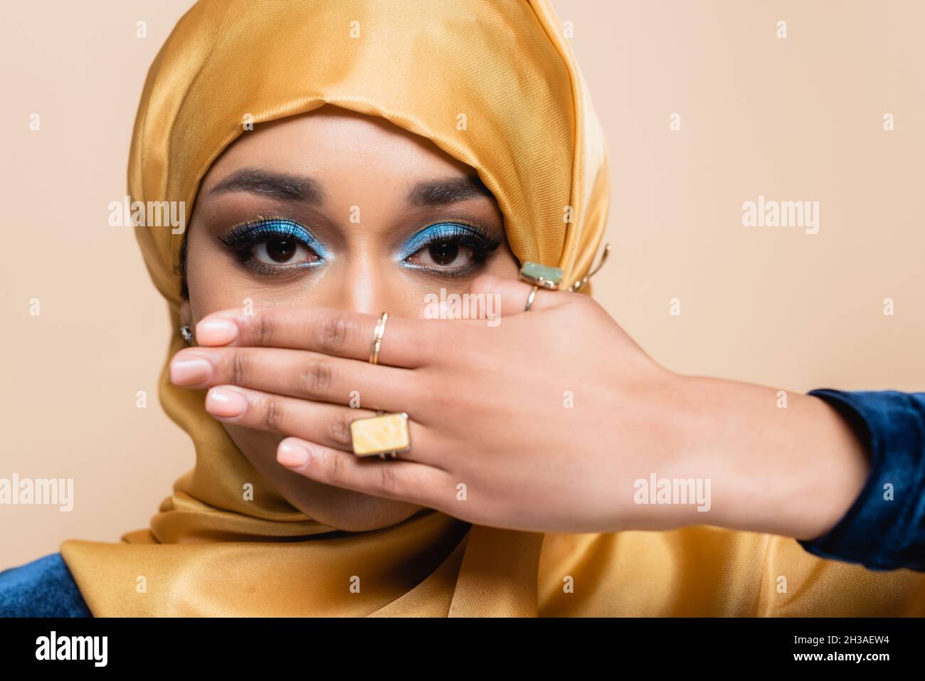 muslim woman in yellow hijab with golden rings on fingers covering face ...