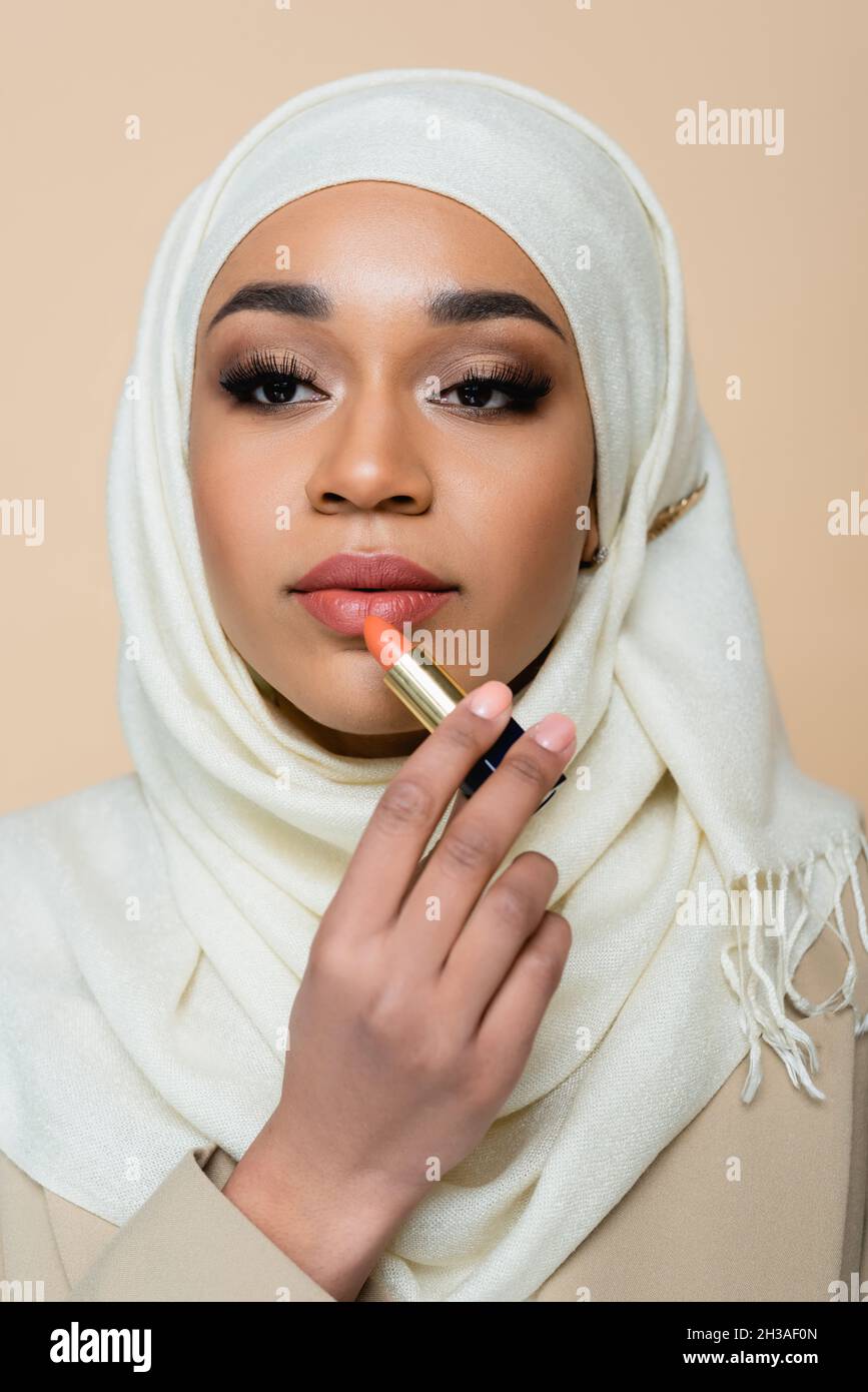 young muslim woman in hijab applying lipstick isolated on beige Stock ...