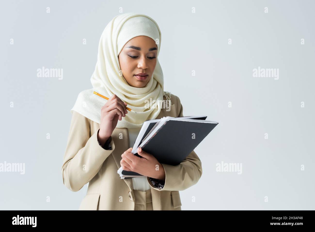 muslim woman in hijab holding pencil and folders isolated on grey Stock ...