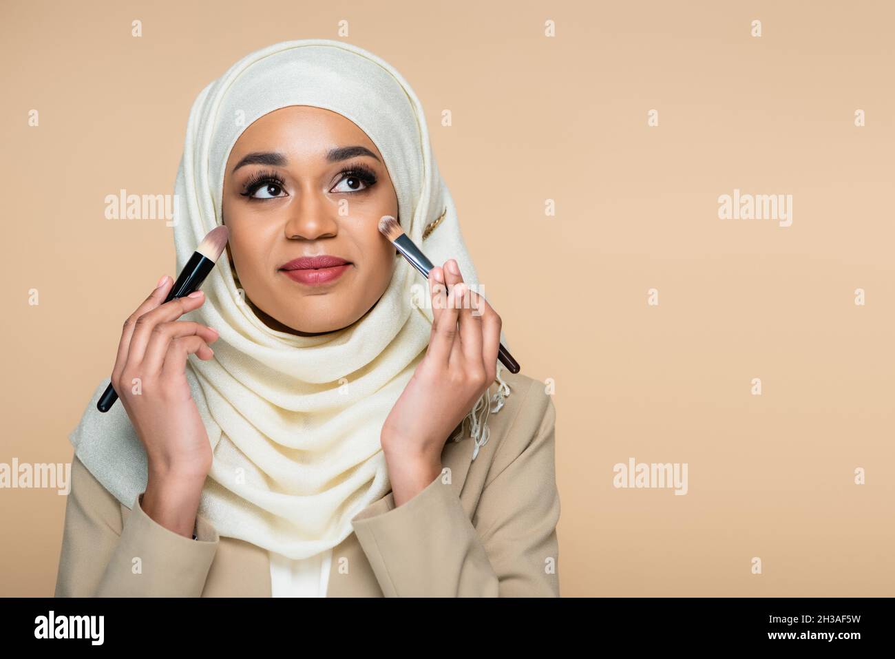 smiling muslim woman in hijab applying face foundation with cosmetic ...