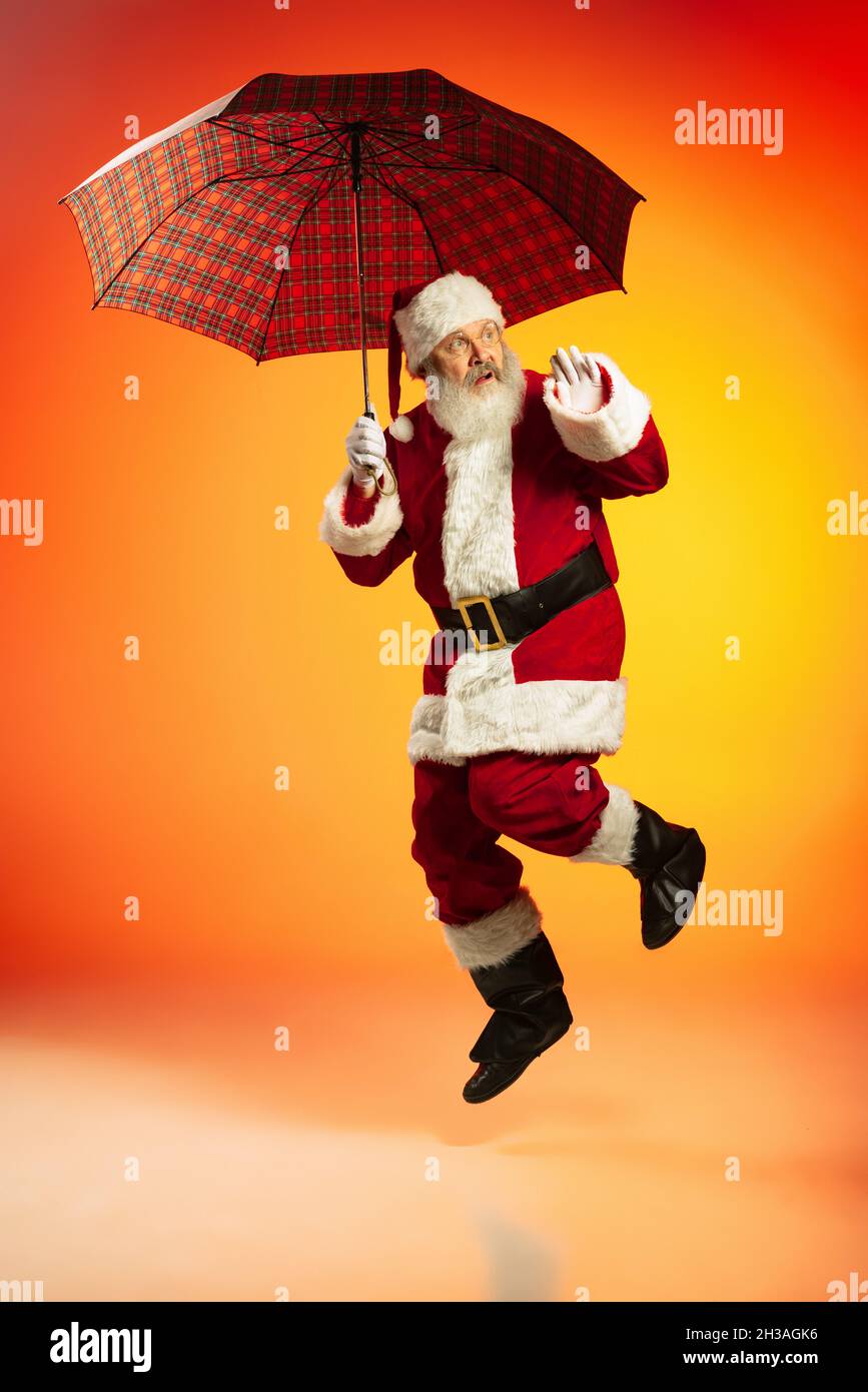 Portrait of emotional Santa Claus with umbrella jumping isolated on red ...