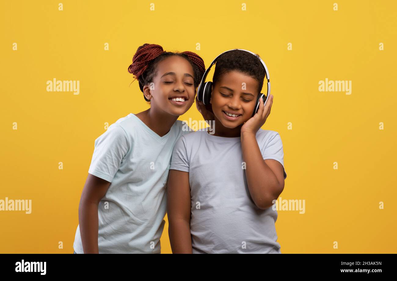 Emotional black siblings with wireless headsets listening to music ...
