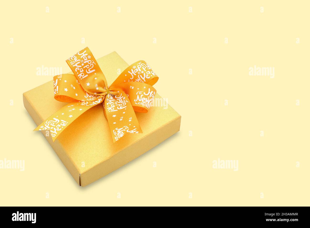 A gold color present box with a bright yellow ribbon on yellow ...