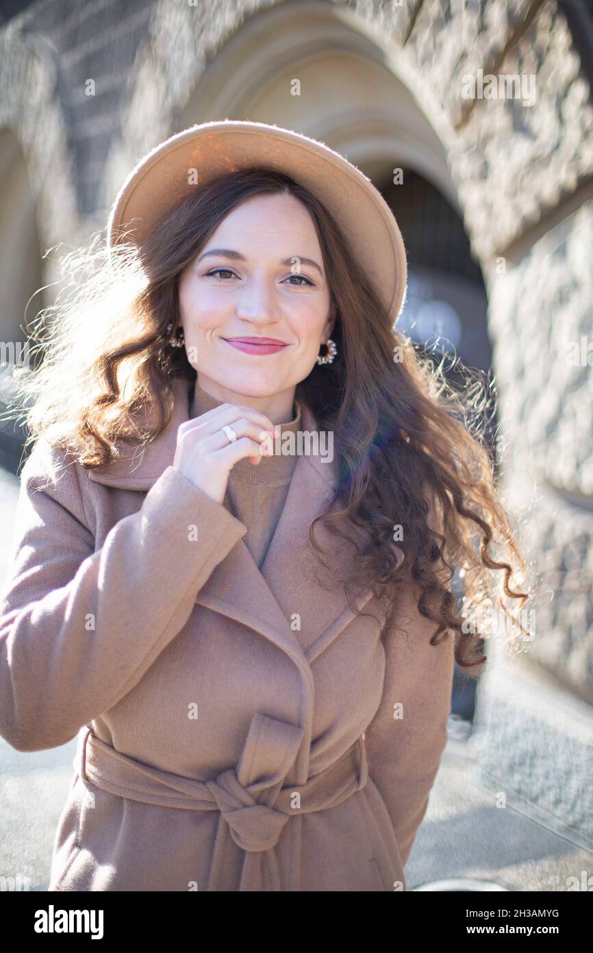 Portrait of smiling pretty woman with curly hair in pastel pink coat ...