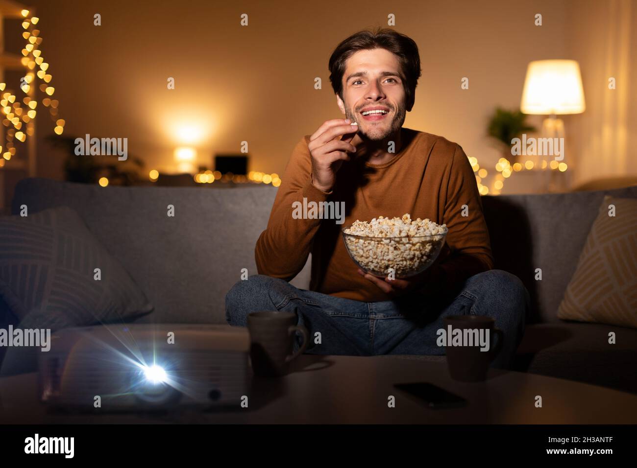 Excited Man Watching Movie Using Projector Eating Popcorn At Home Stock Photo - Alamy