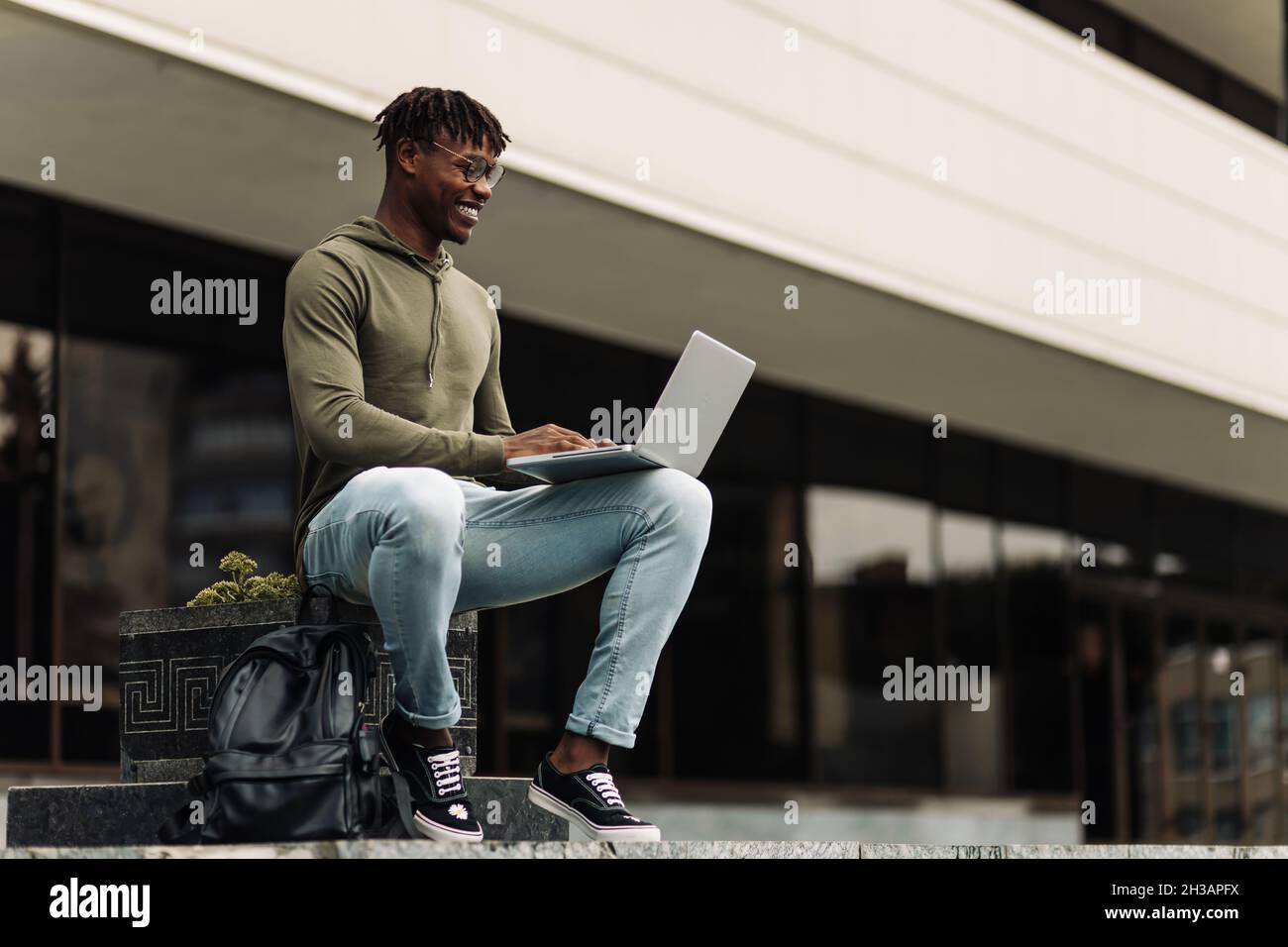 African black man working on a city street on a bench, uses a laptop ...