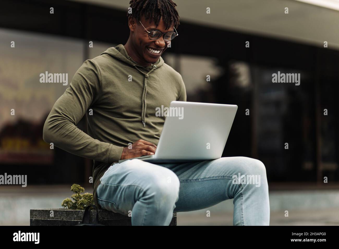 African black man working on a city street on a bench, uses a laptop ...