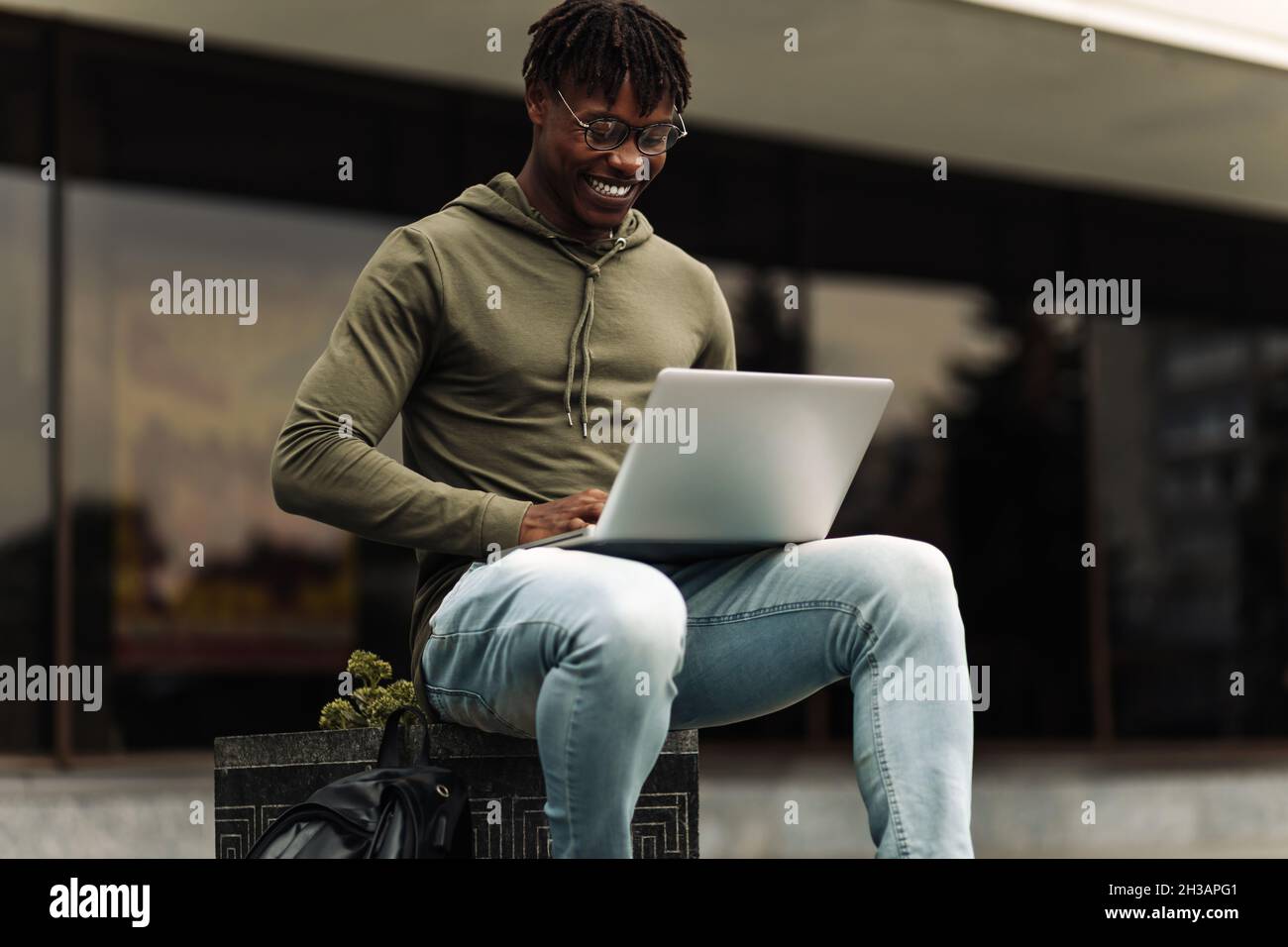 African black man working on a city street on a bench, uses a laptop ...