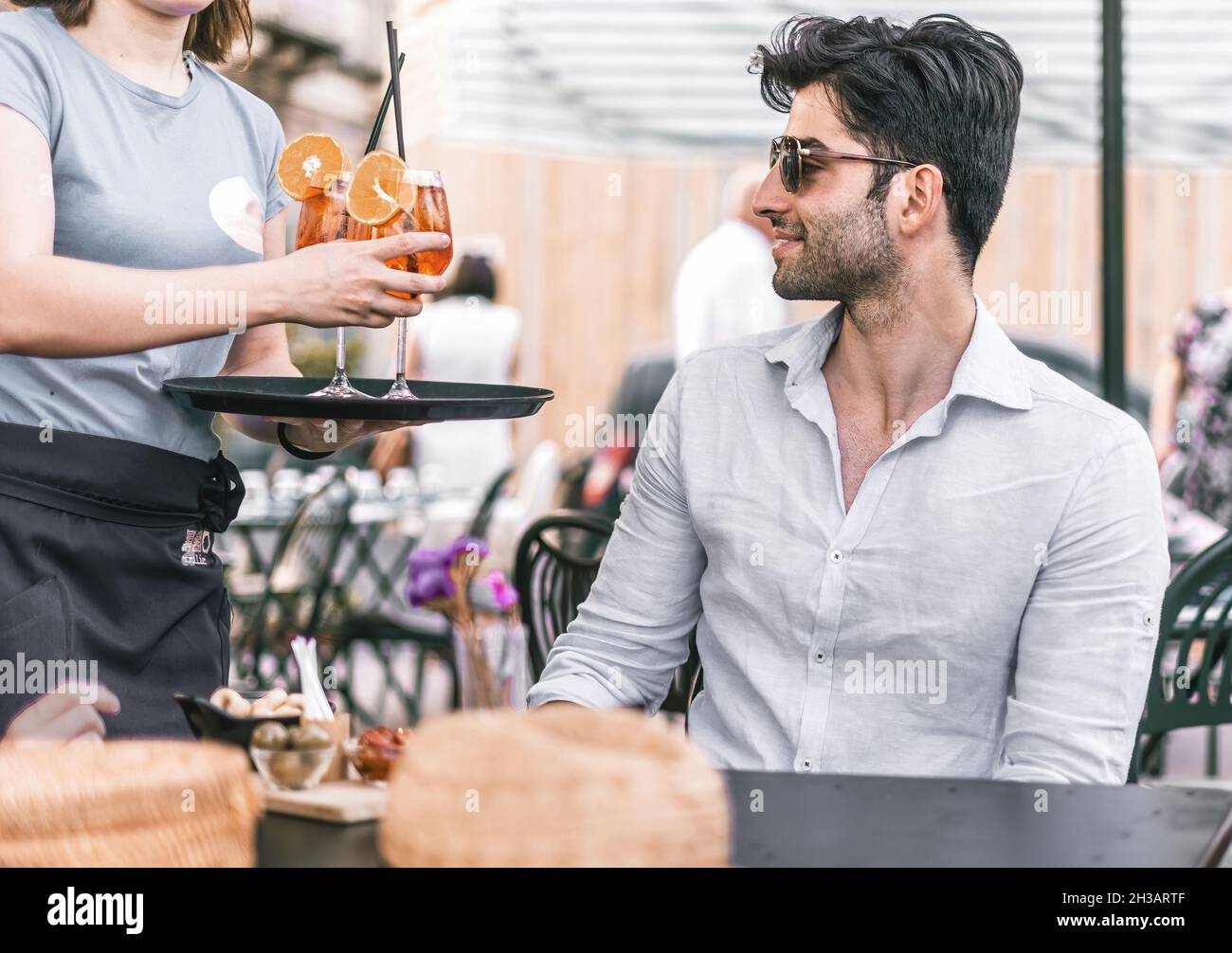 A young man sitting at a bar table receives a cocktail from the waiter ...