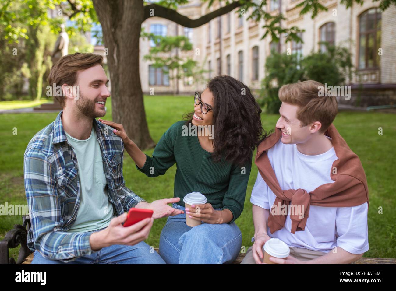 Three friends spending time in the park and talking Stock Photo - Alamy