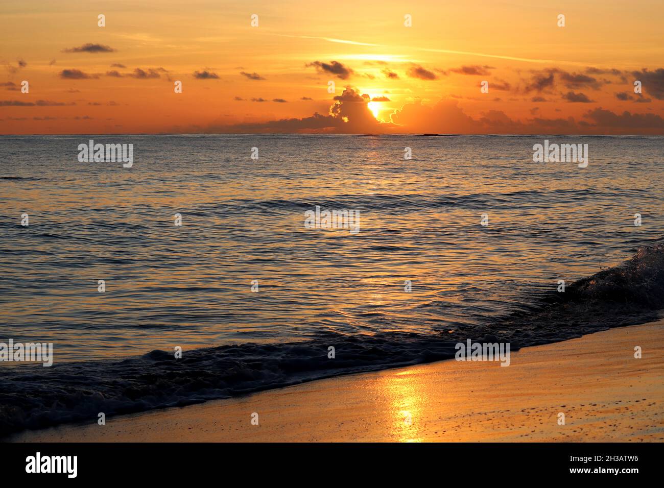 Sunset on a sandy beach, orange sun is shining through the clouds ...