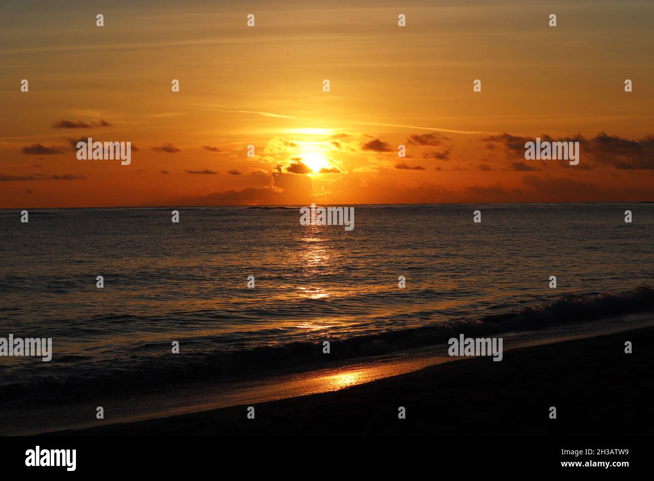 Sunset on a sandy beach, orange sun is shining through the clouds ...