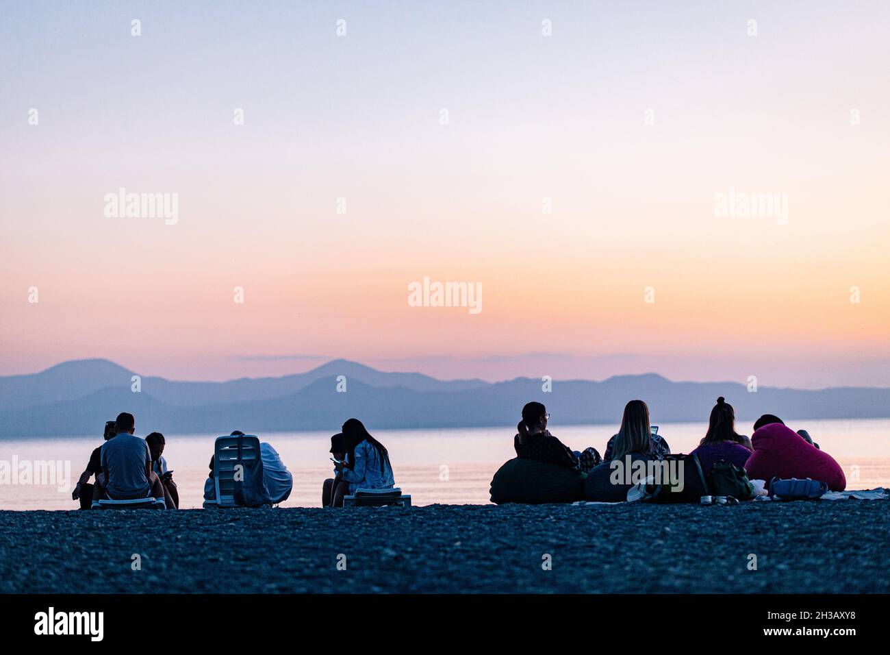 Back view of a group of friends sitting on the beach overlooking the tranquil Lake Sevan at ...