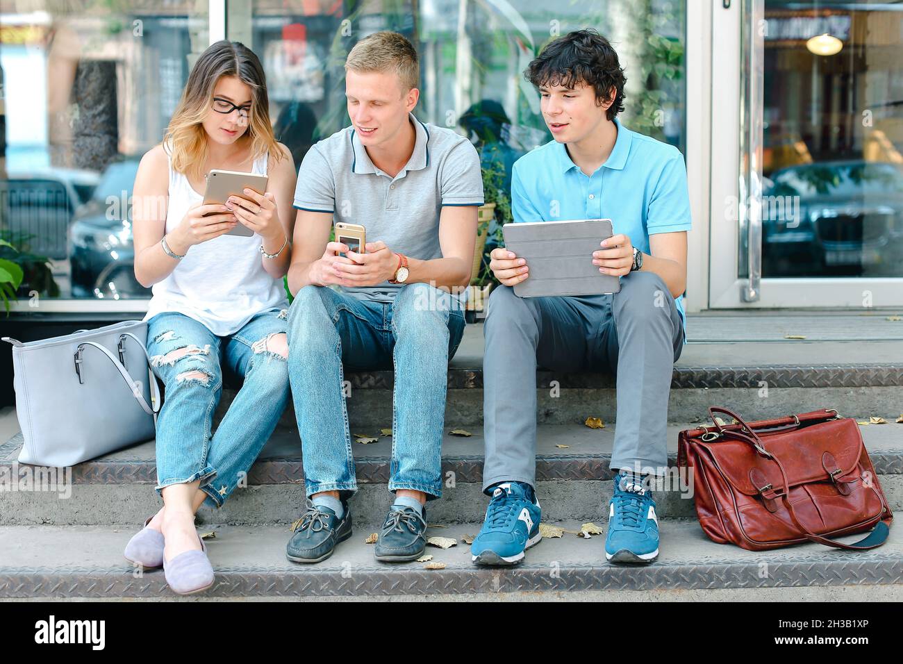 Young three friends sitting floor in the street, talking, using Stock ...
