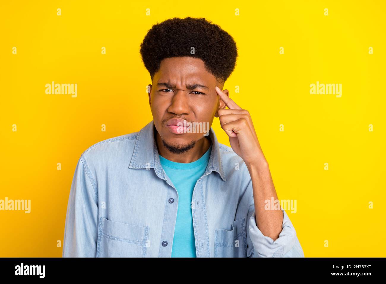 Photo of confused cute dark skin man wear jeans shirt finger temple ...