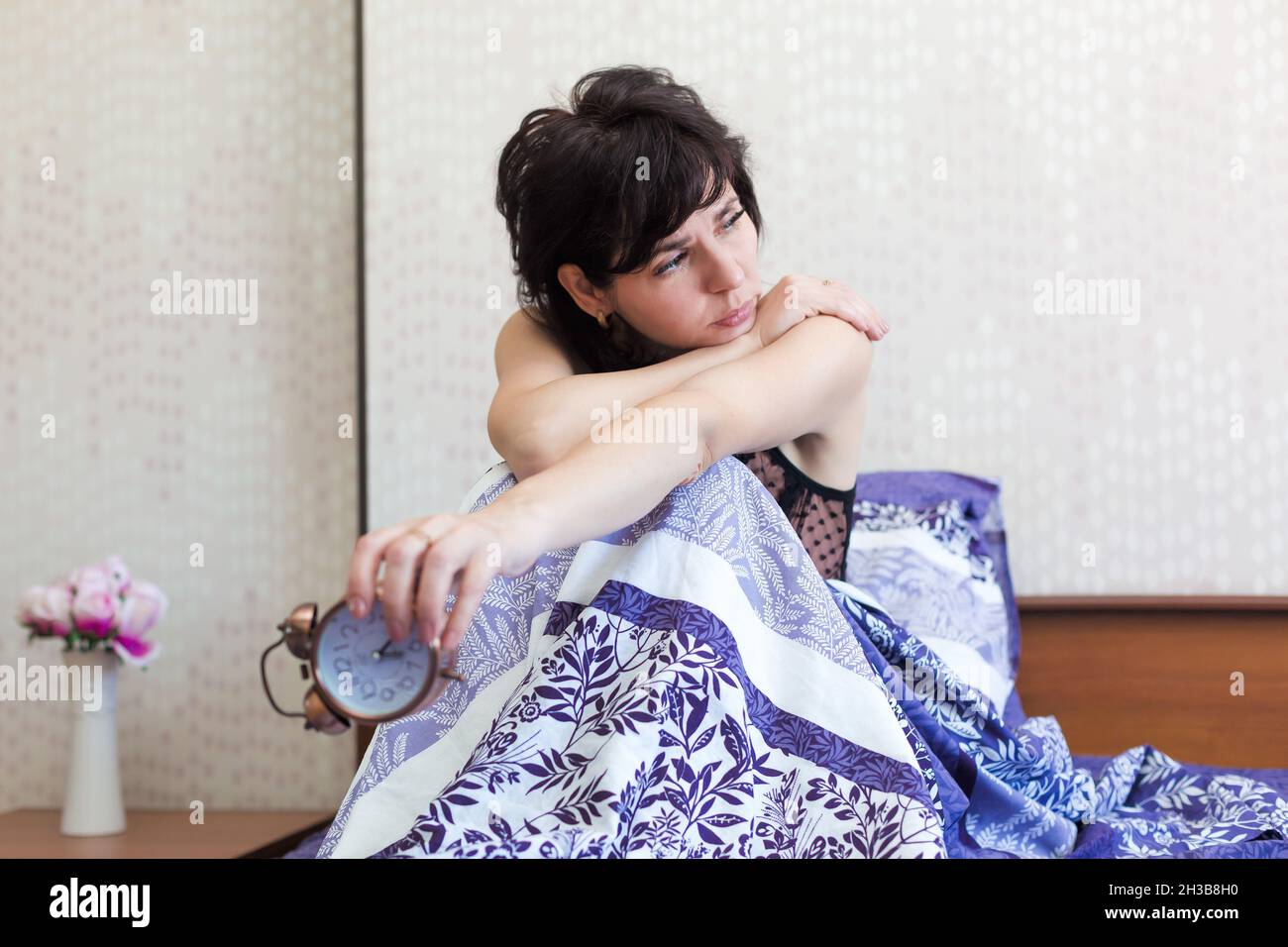 A sleepy, sleepy woman with an alarm clock in her hand is sitting on ...