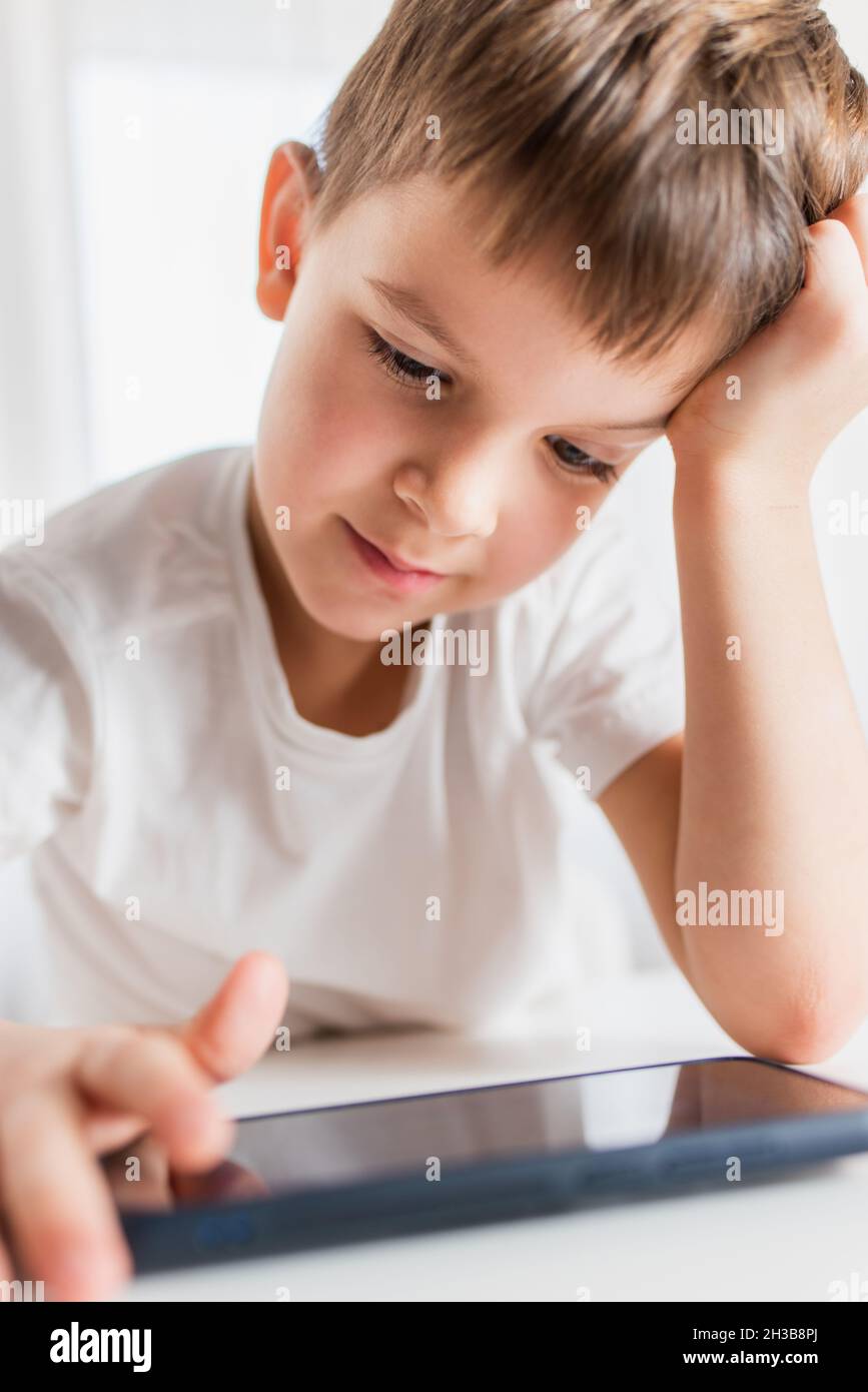 A little boy in a white T-shirt plays games on the phone at home. A ...