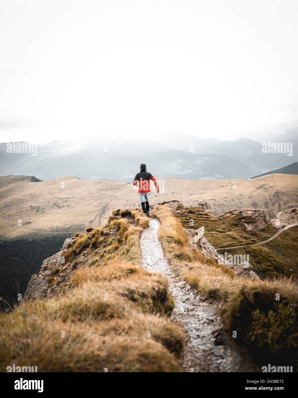 Man in red jacket waliking on a mountain path Stock Photo - Alamy