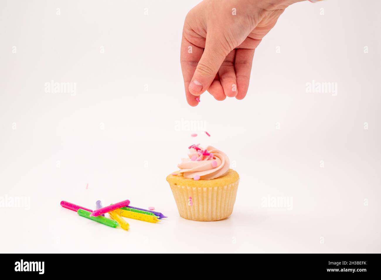 Child's hand decorating a pink cupcake with sprinkles Stock Photo - Alamy