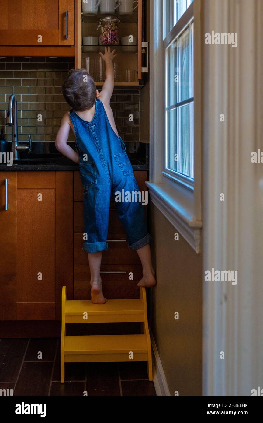 Boy on a step stool reaching for a jar of lollipops Stock Photo - Alamy