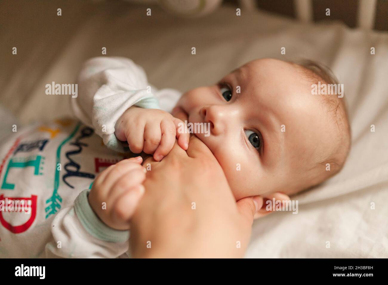 Infant baby biting hand of mother while teething Stock Photo - Alamy